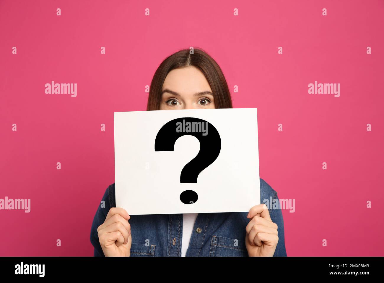 Emotional woman holding question mark sign on pink background Stock ...