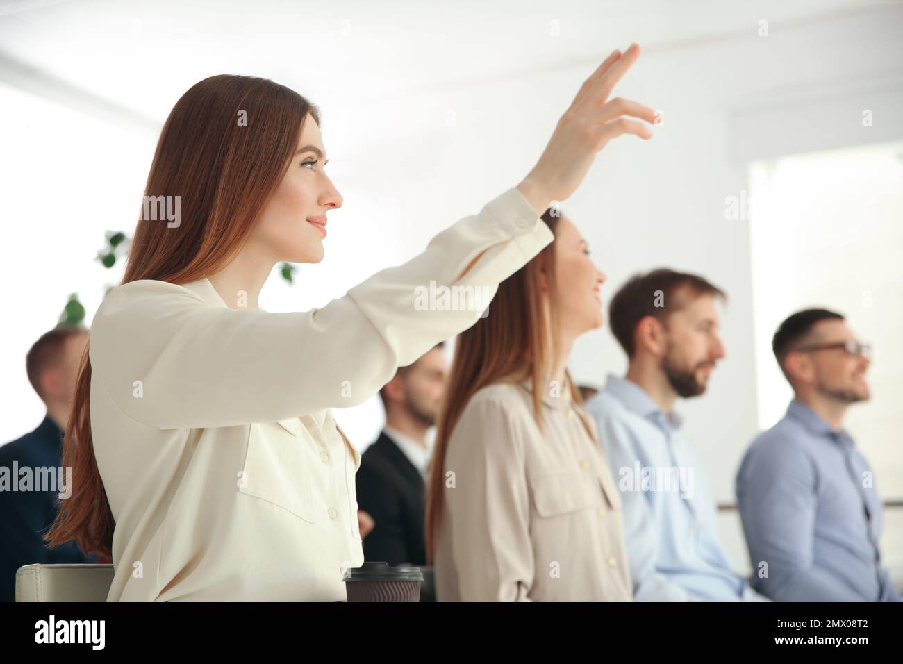 Young woman raising hand to ask question at business training indoors ...