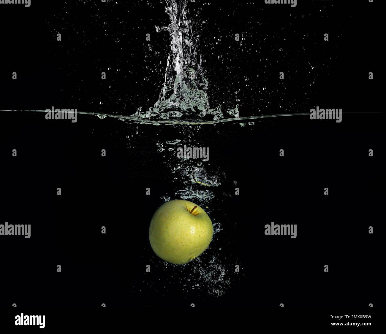Ripe apple falling down into clear water with splashes against black ...