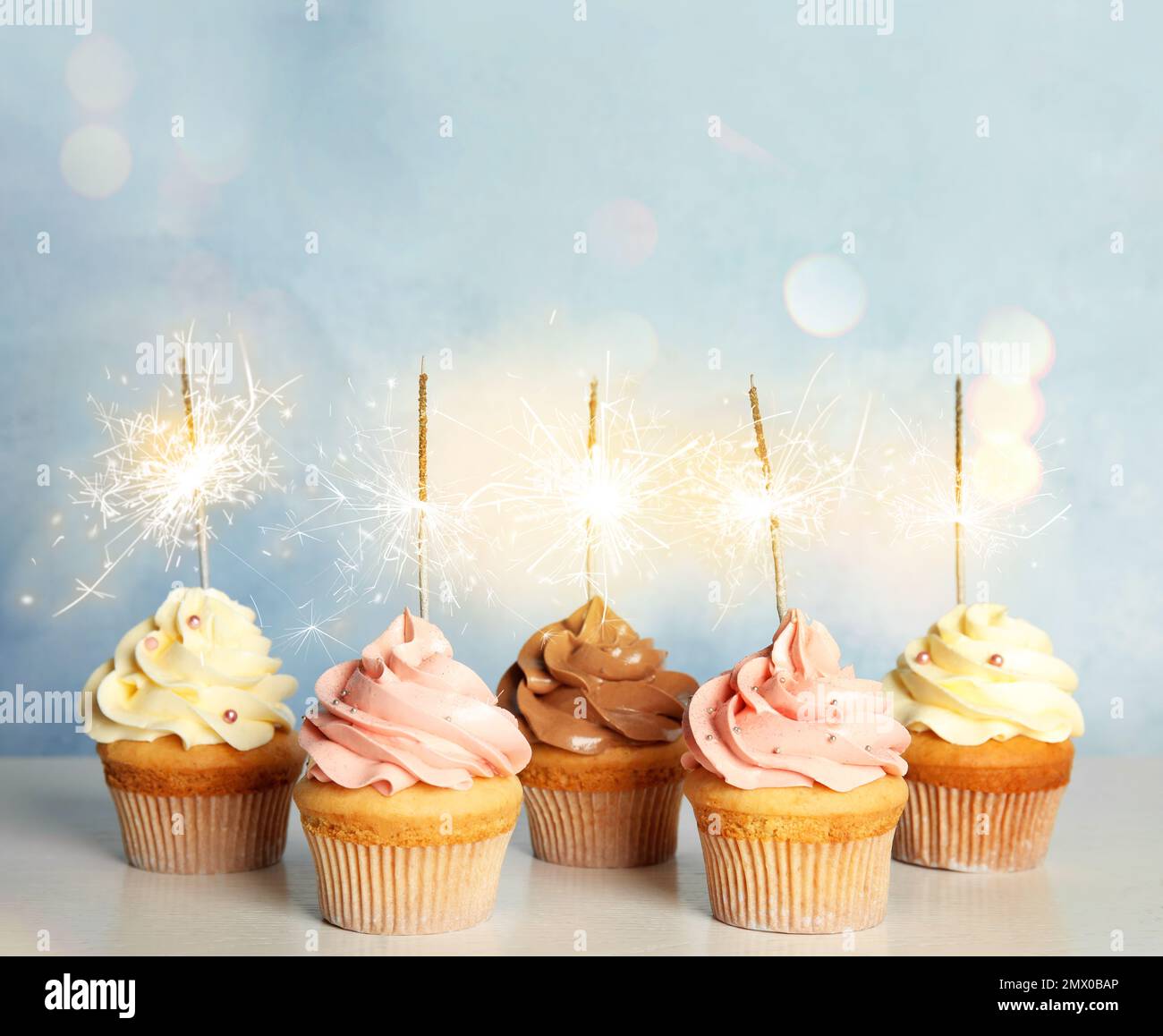 Birthday cupcakes with sparklers on table against light blue background Stock Photo - Alamy