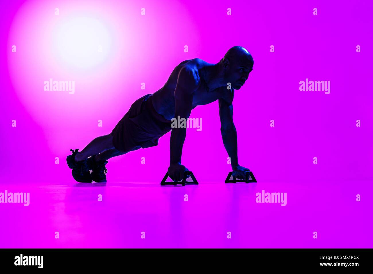 Athletic man is doing push ups while using special handles on studio ...