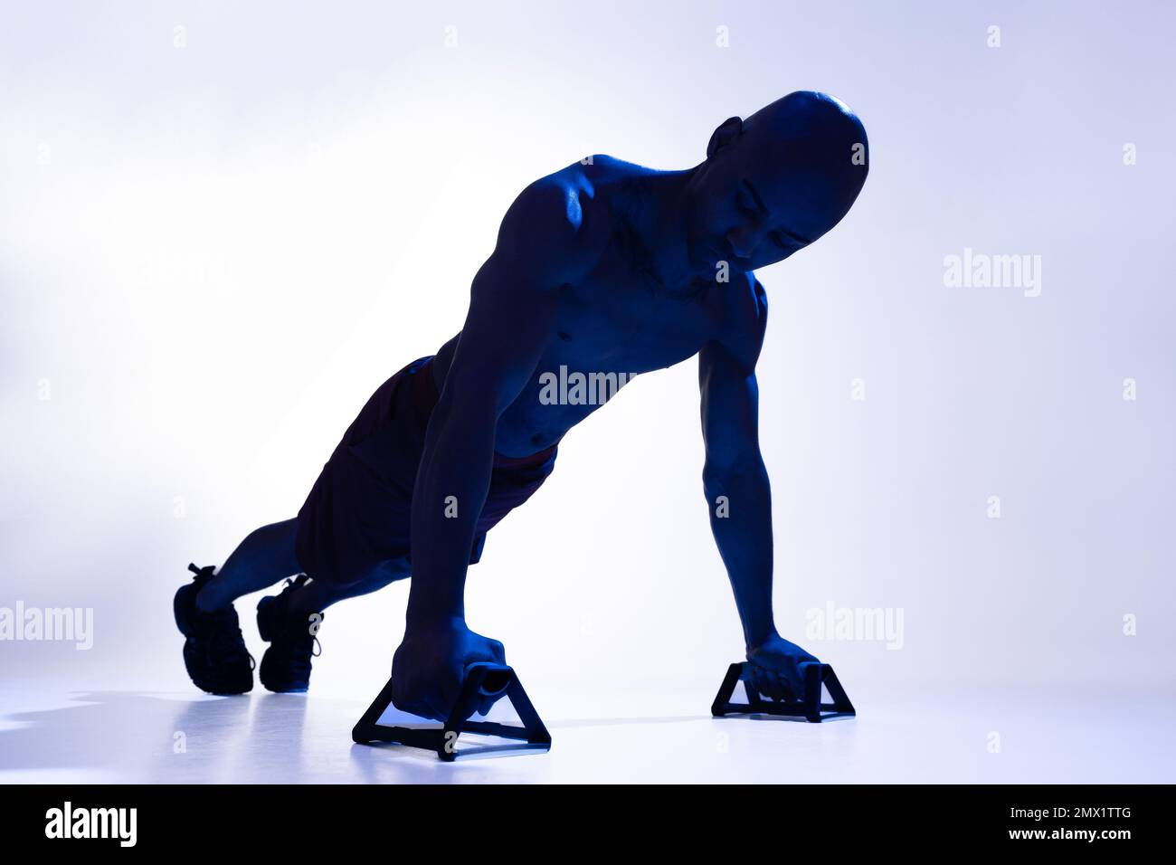 Athletic man is doing push ups while using special handles on studio ...