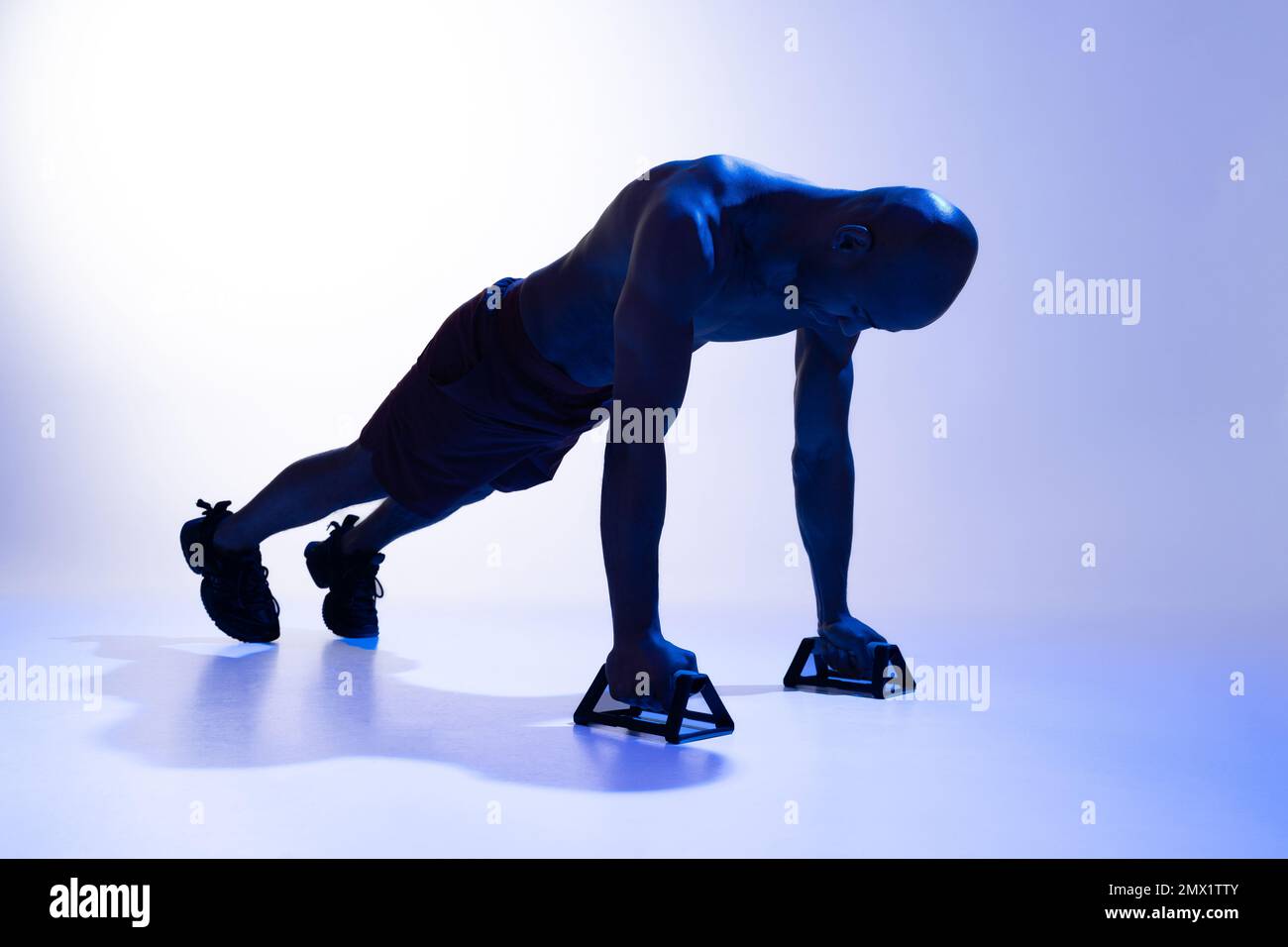 Athletic man is doing push ups while using special handles on studio ...