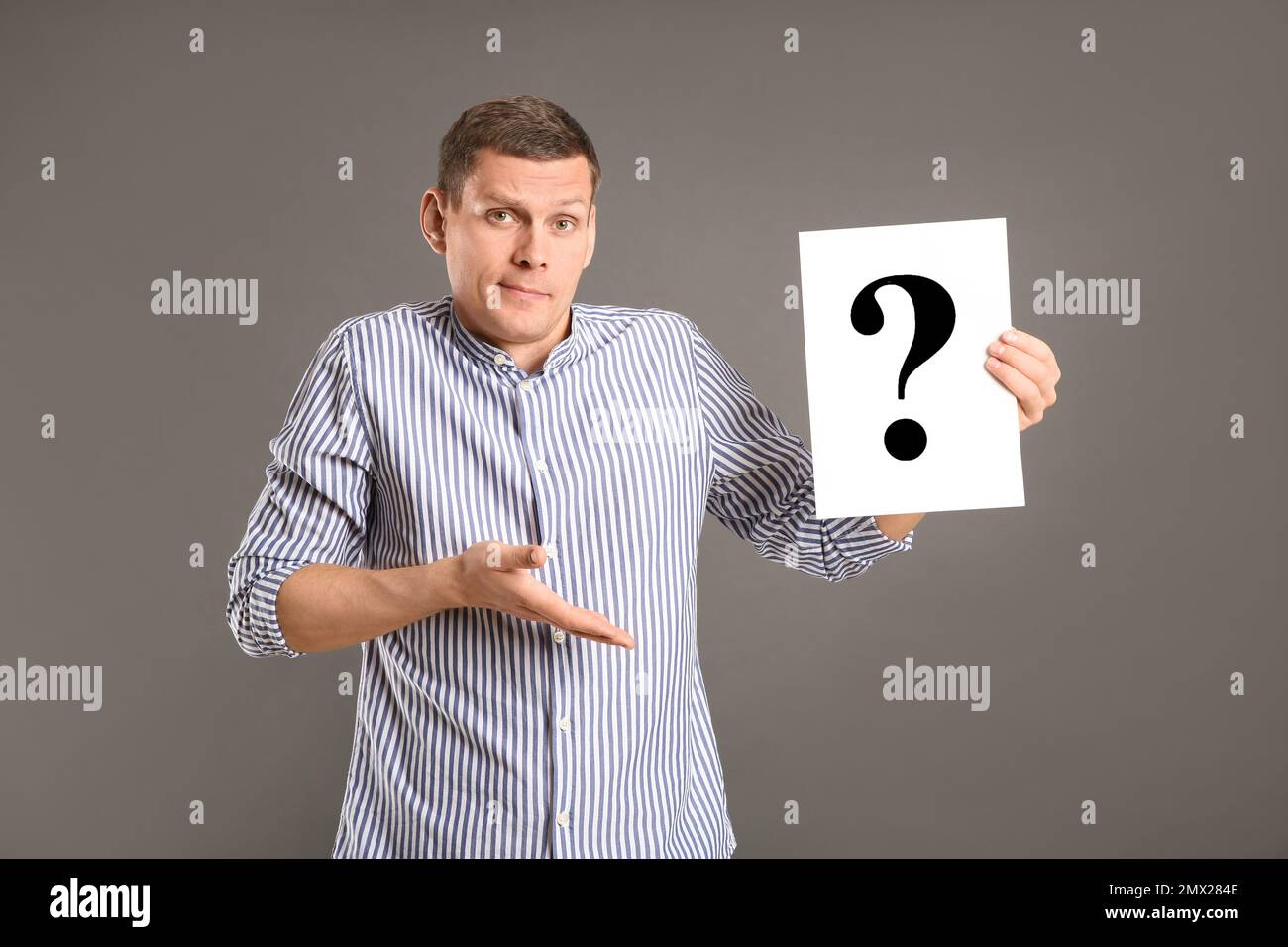 Emotional man holding paper with question mark on grey background Stock ...