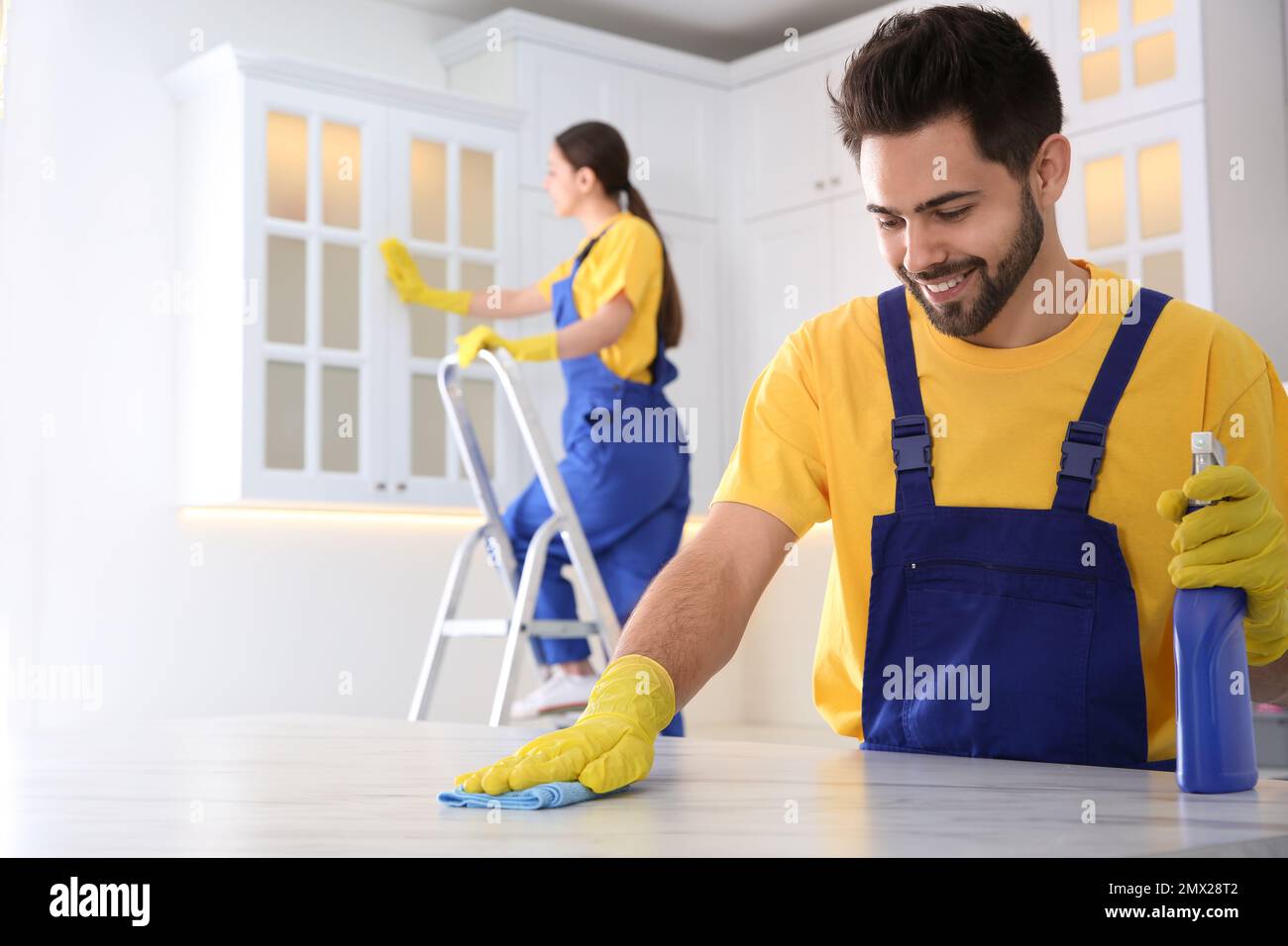 Professional young janitor cleaning table in kitchen Stock Photo - Alamy
