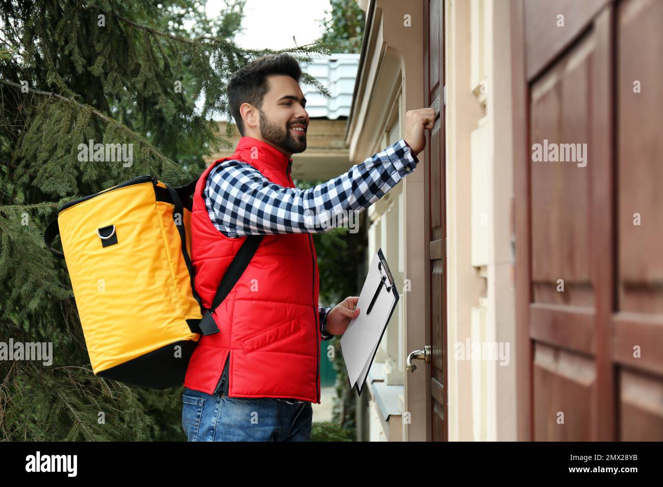 Courier with thermo bag and clipboard knocking on customer's house ...