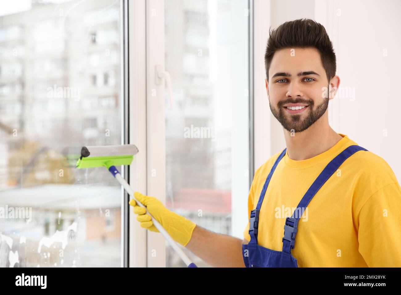 Professional young janitor in uniform cleaning window indoors Stock ...