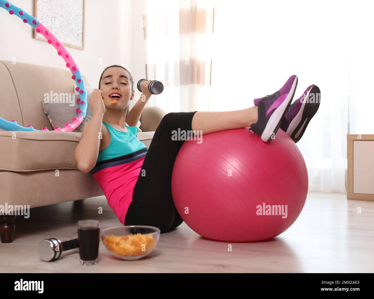 Lazy young woman with sport equipment eating junk food at home Stock ...