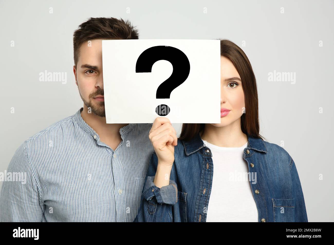 Couple holding question mark sign on light background Stock Photo - Alamy