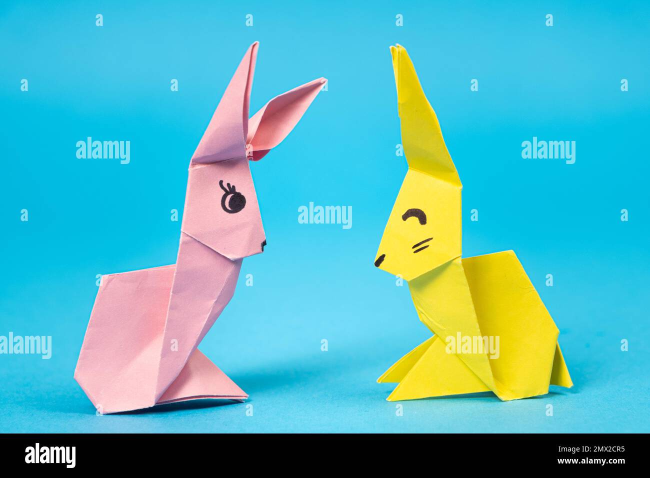 A pink and yellow origami rabbits on a blue background. Crafts for ...