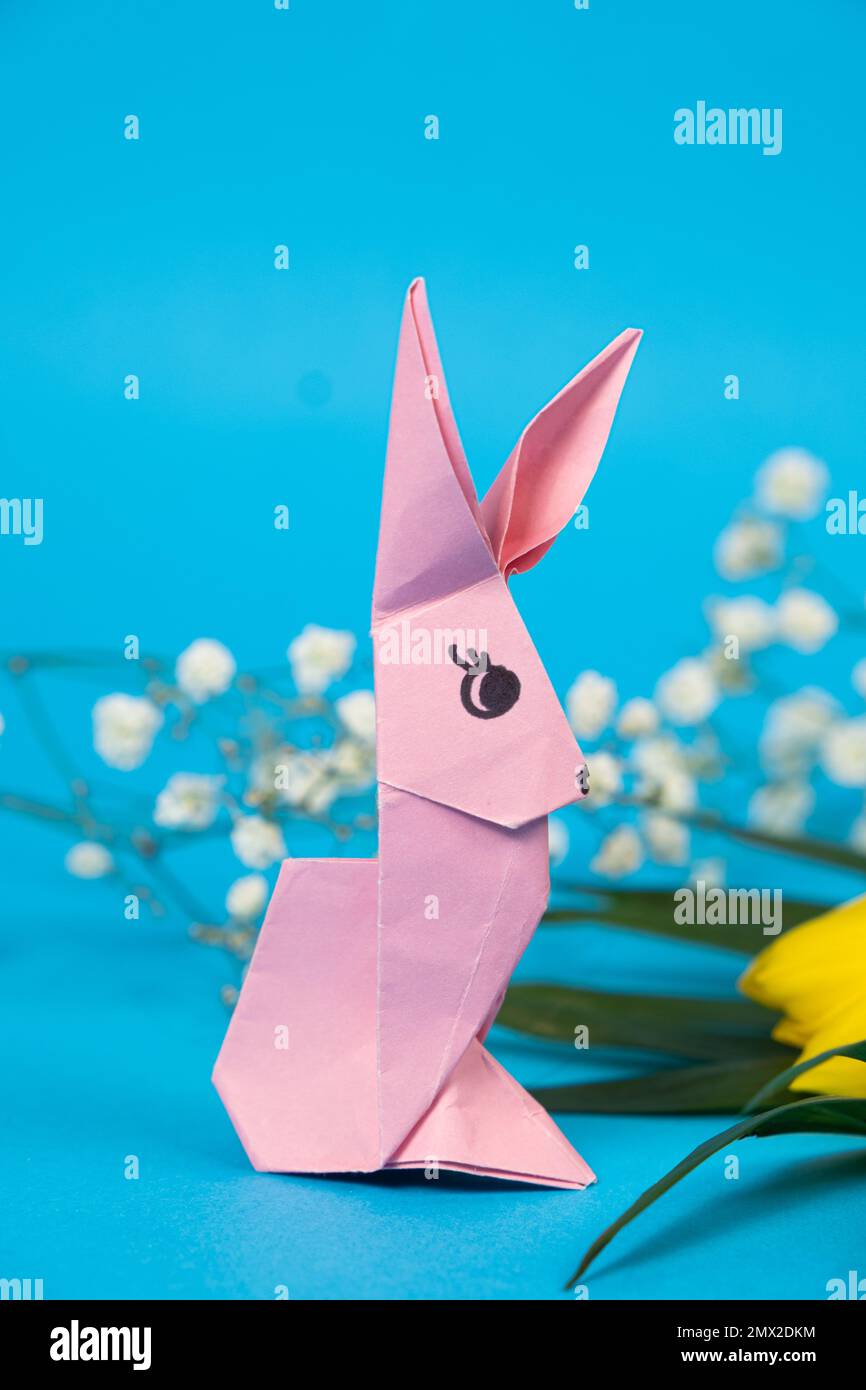 A pink origami rabbit on a blue background. Crafts for Easter, fold ...
