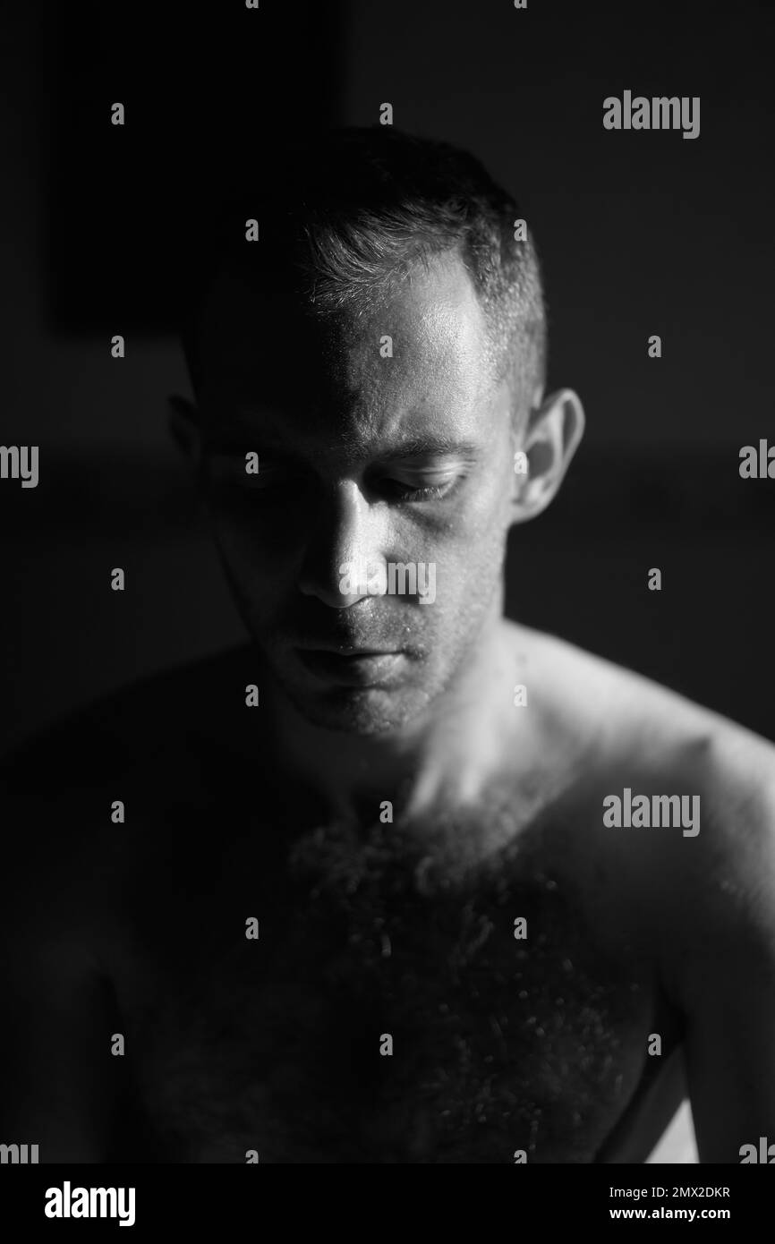 Portrait of handsome man in hard side light meditating. Half of male ...
