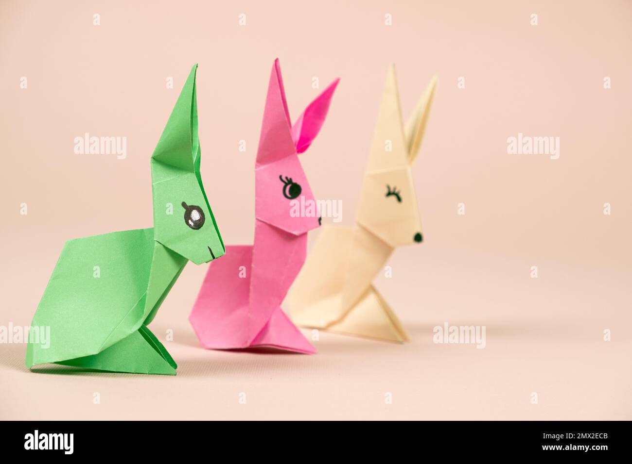 Three paper origami bunnies and an Easter egg on a beige background ...