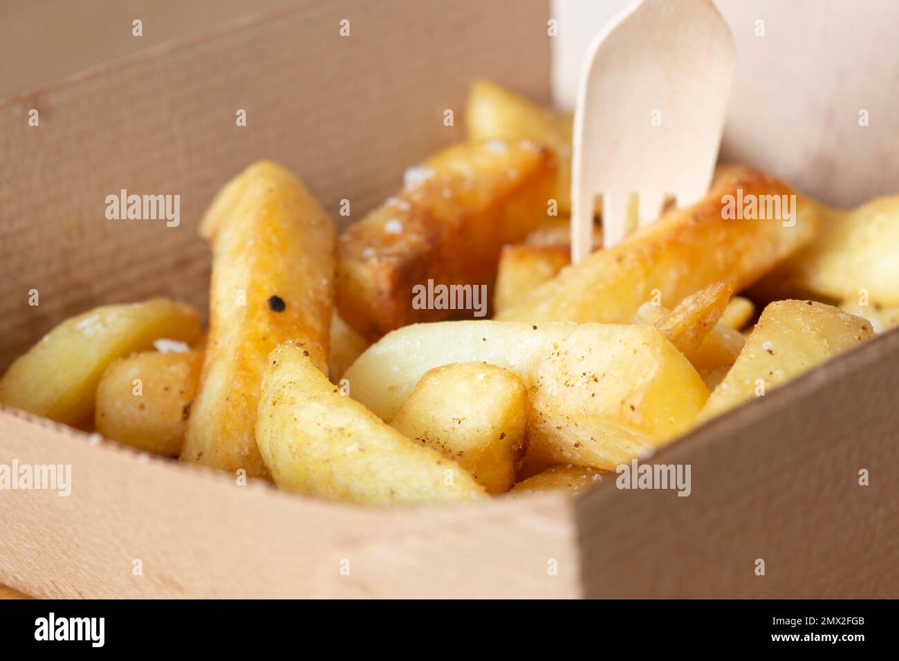 Chip shop chips takeaway in a cardboard tray with a wooden fork ...