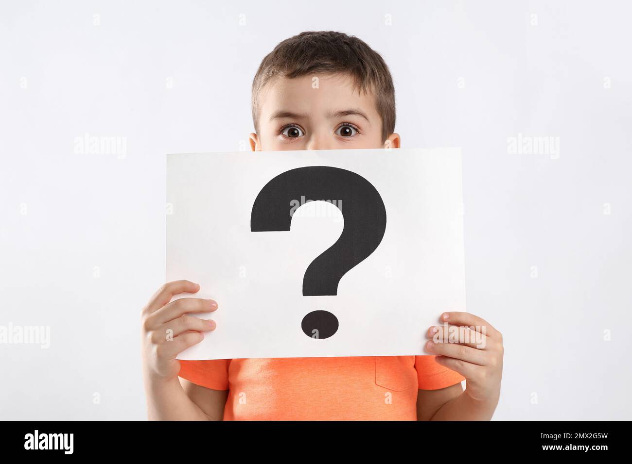 Emotional little boy holding paper with question mark on white ...