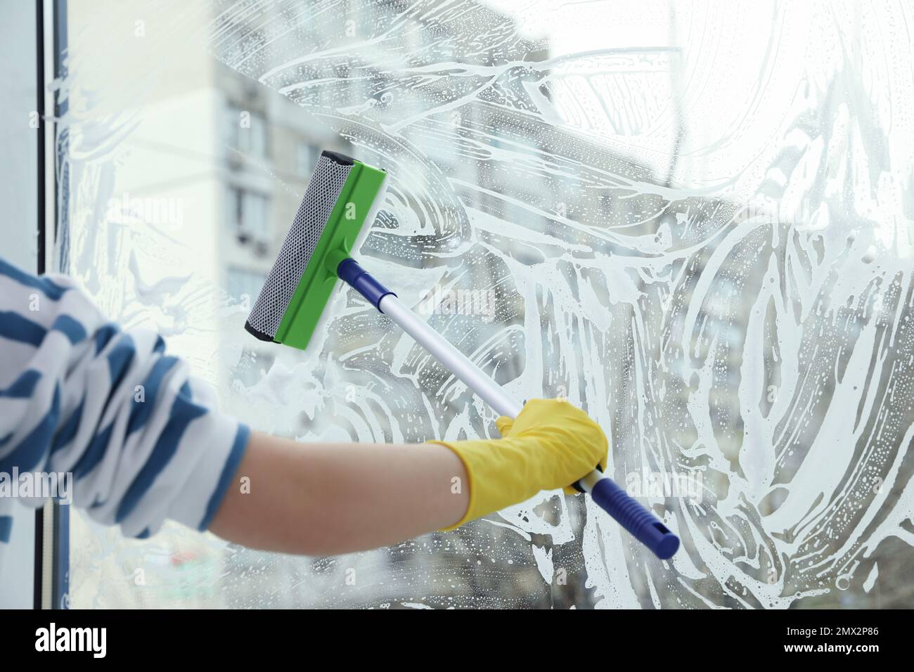 Woman cleaning window with squeegee at home, closeup. Space for text ...