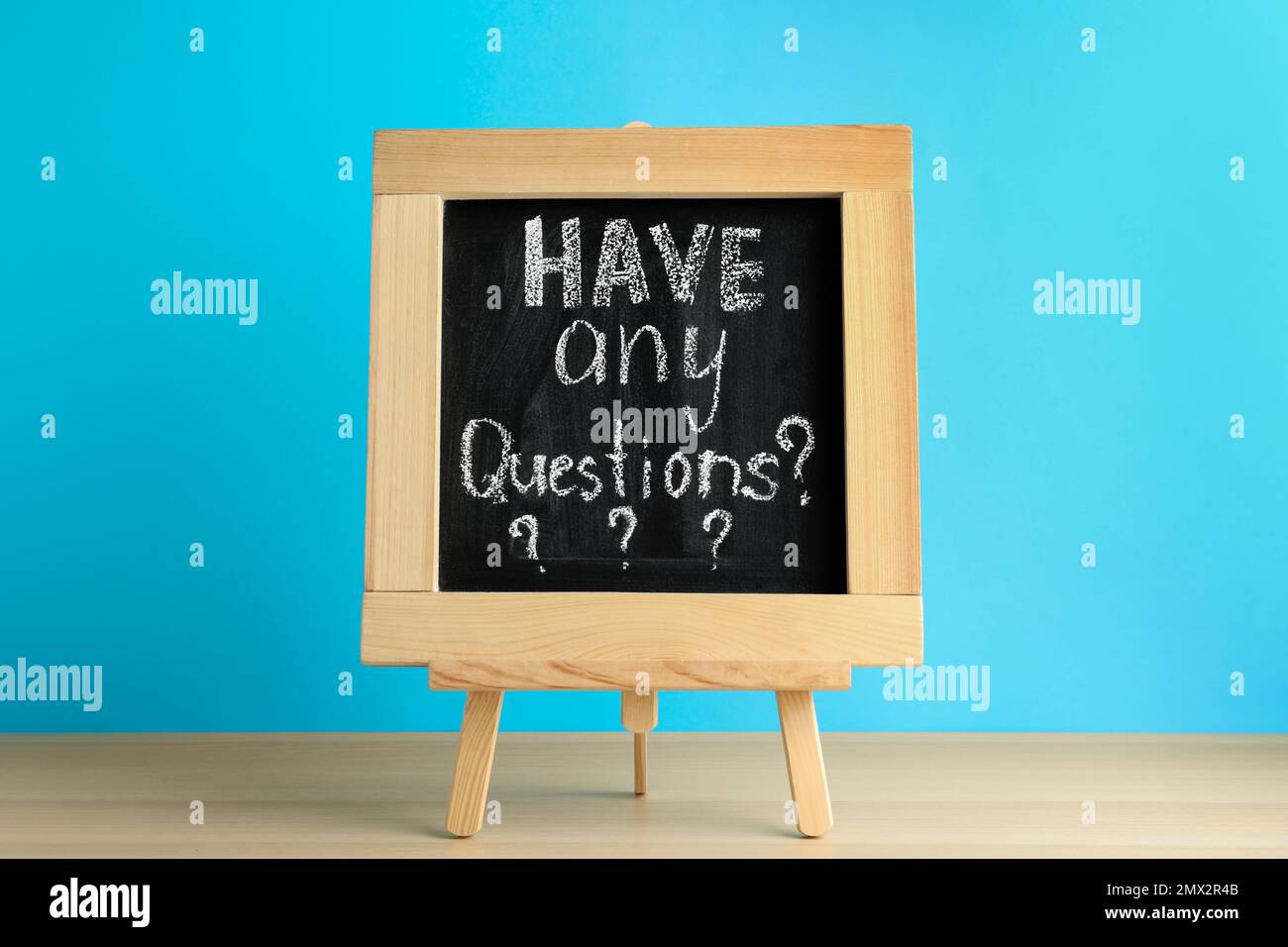 Blackboard with phrase HAVE ANY QUESTIONS on wooden table against blue ...