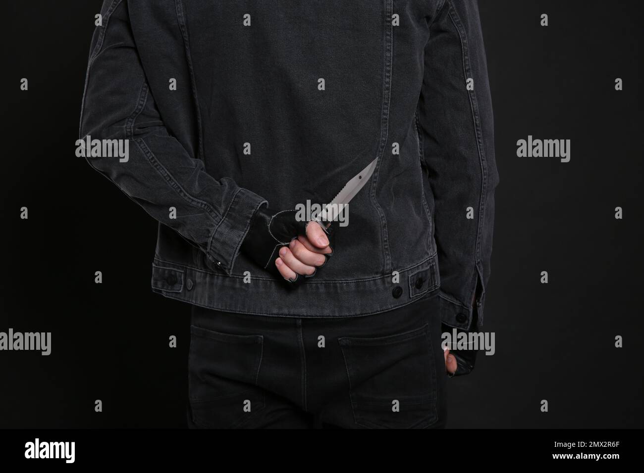 Man with knife behind his back on black background, closeup. Dangerous ...