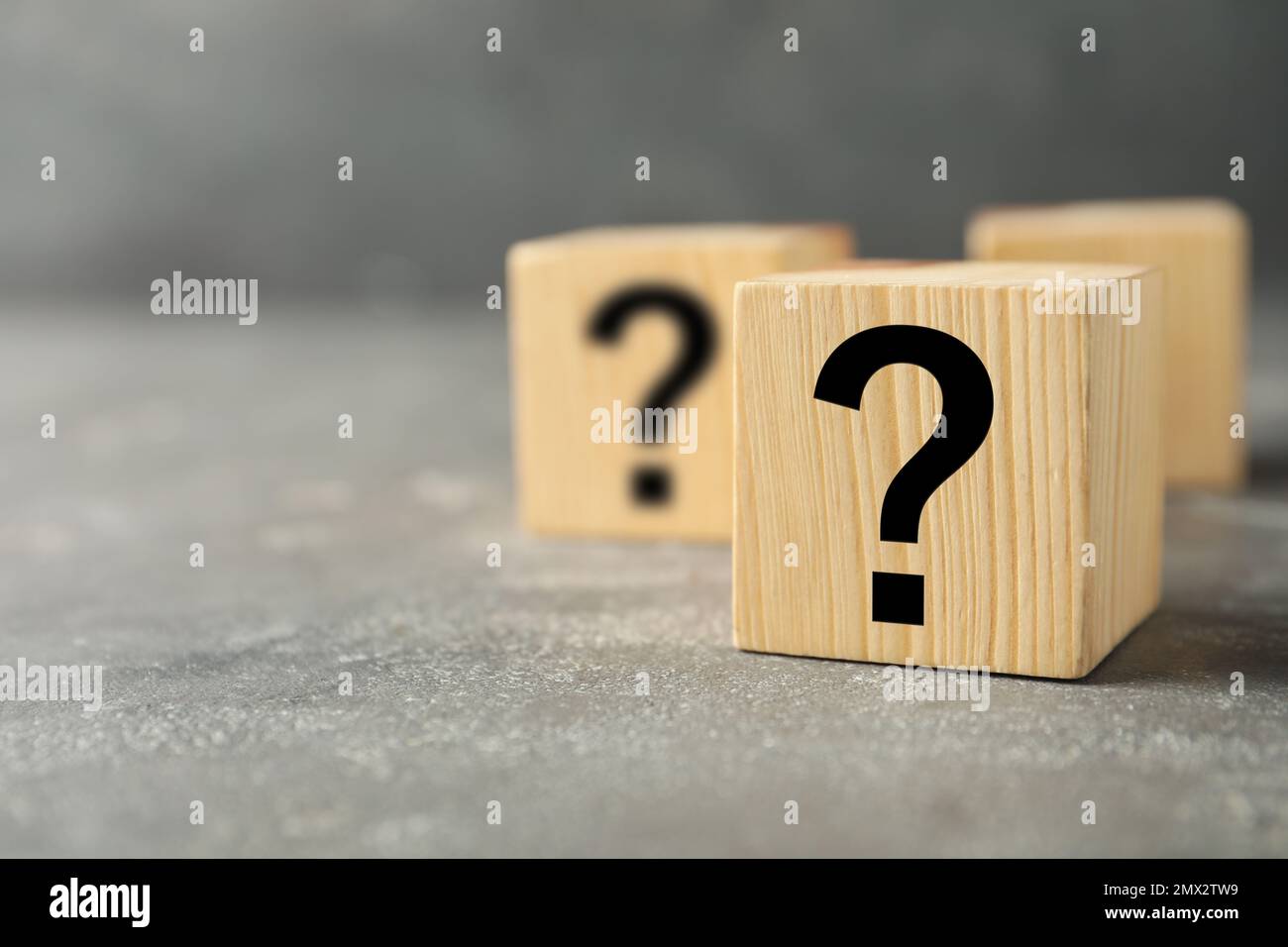 Cube with question mark on grey stone table, closeup. Space for text ...