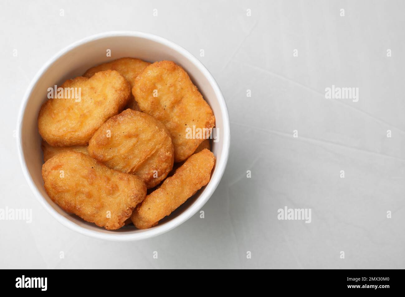 Bucket with tasty chicken nuggets on light grey table, top view. Space ...
