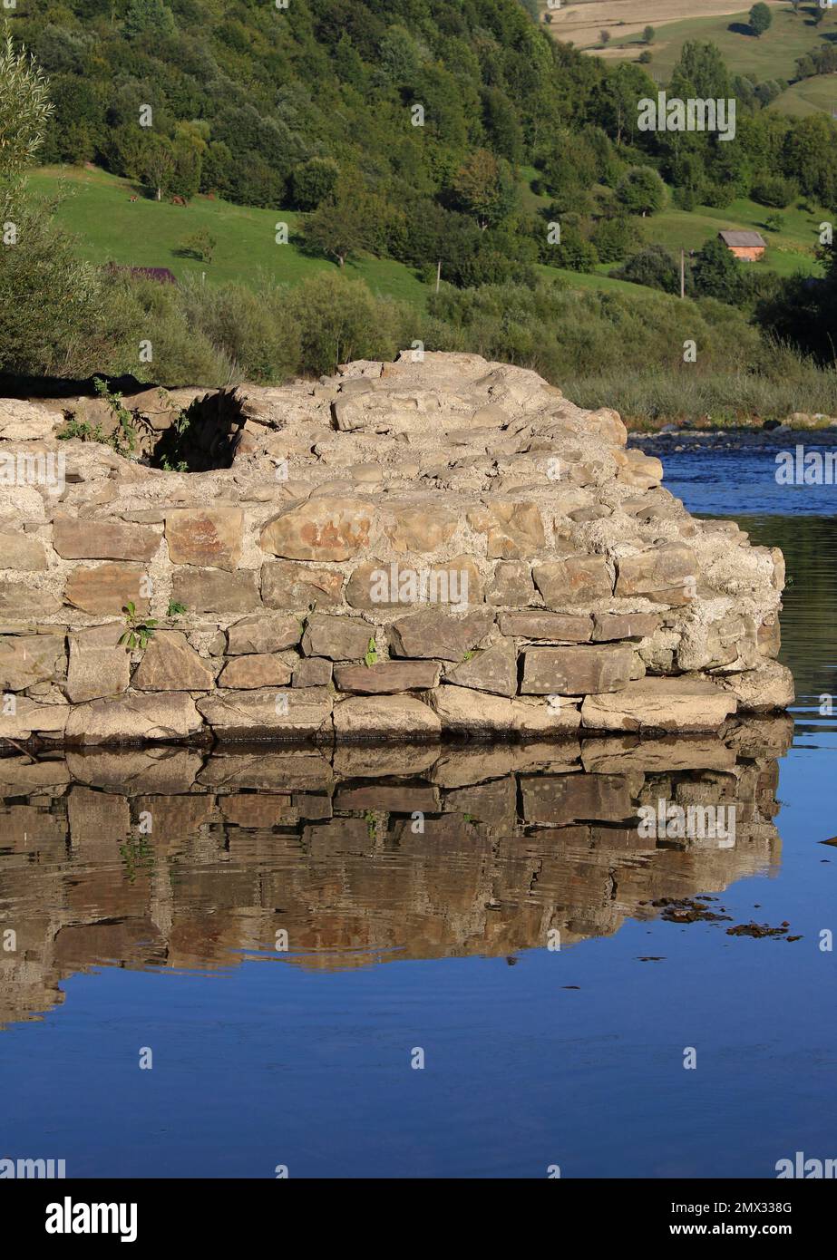 The ruins of an ancient rocky wall are reflected on the water surface ...