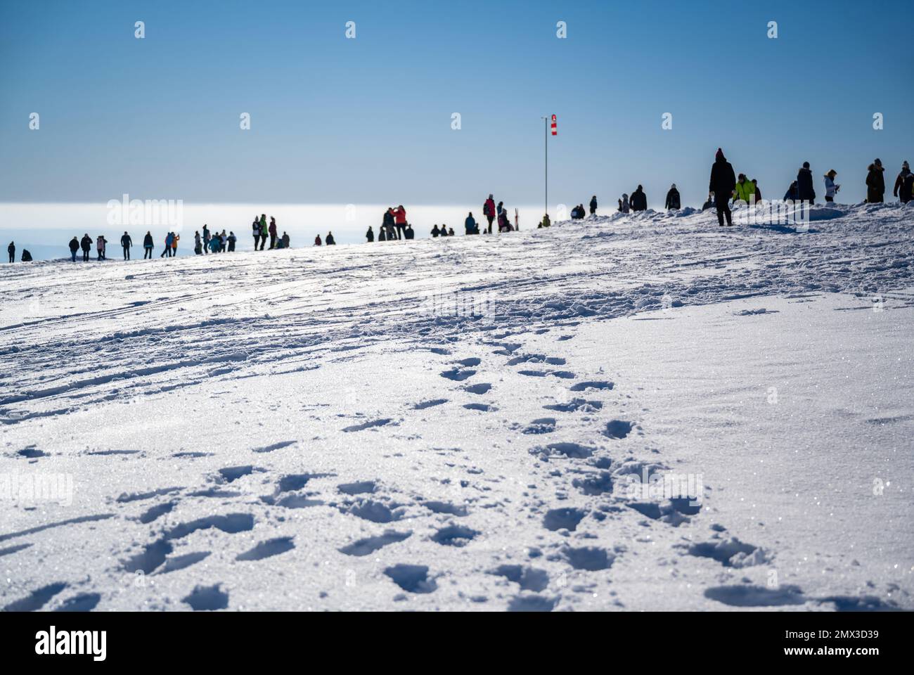 Snowy hillock with track, many (blurry) people silhouette and windsock ...