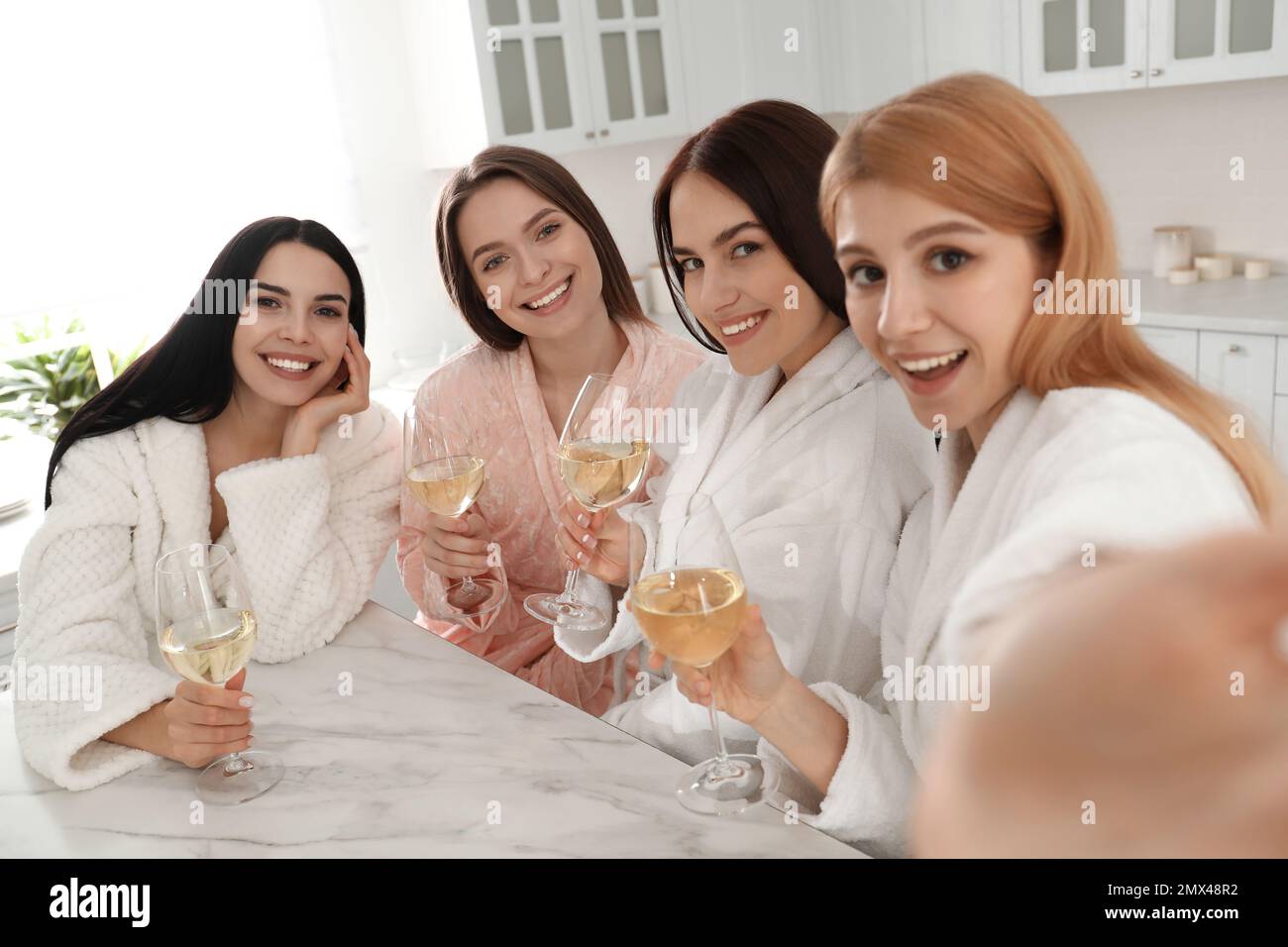 Beautiful young ladies with wine taking selfie in kitchen at pamper ...