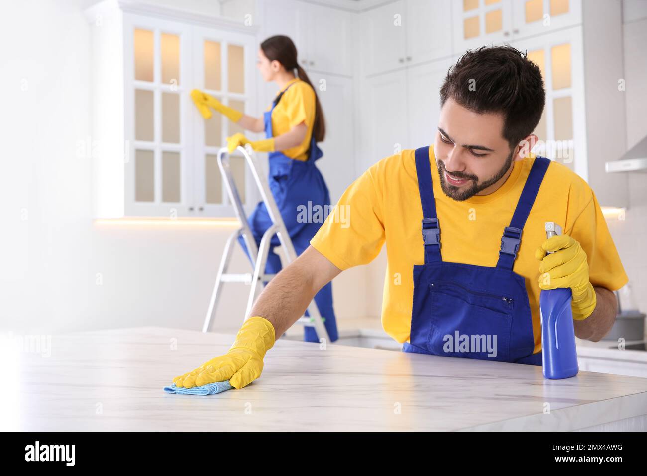 Professional young janitor cleaning table in kitchen Stock Photo - Alamy