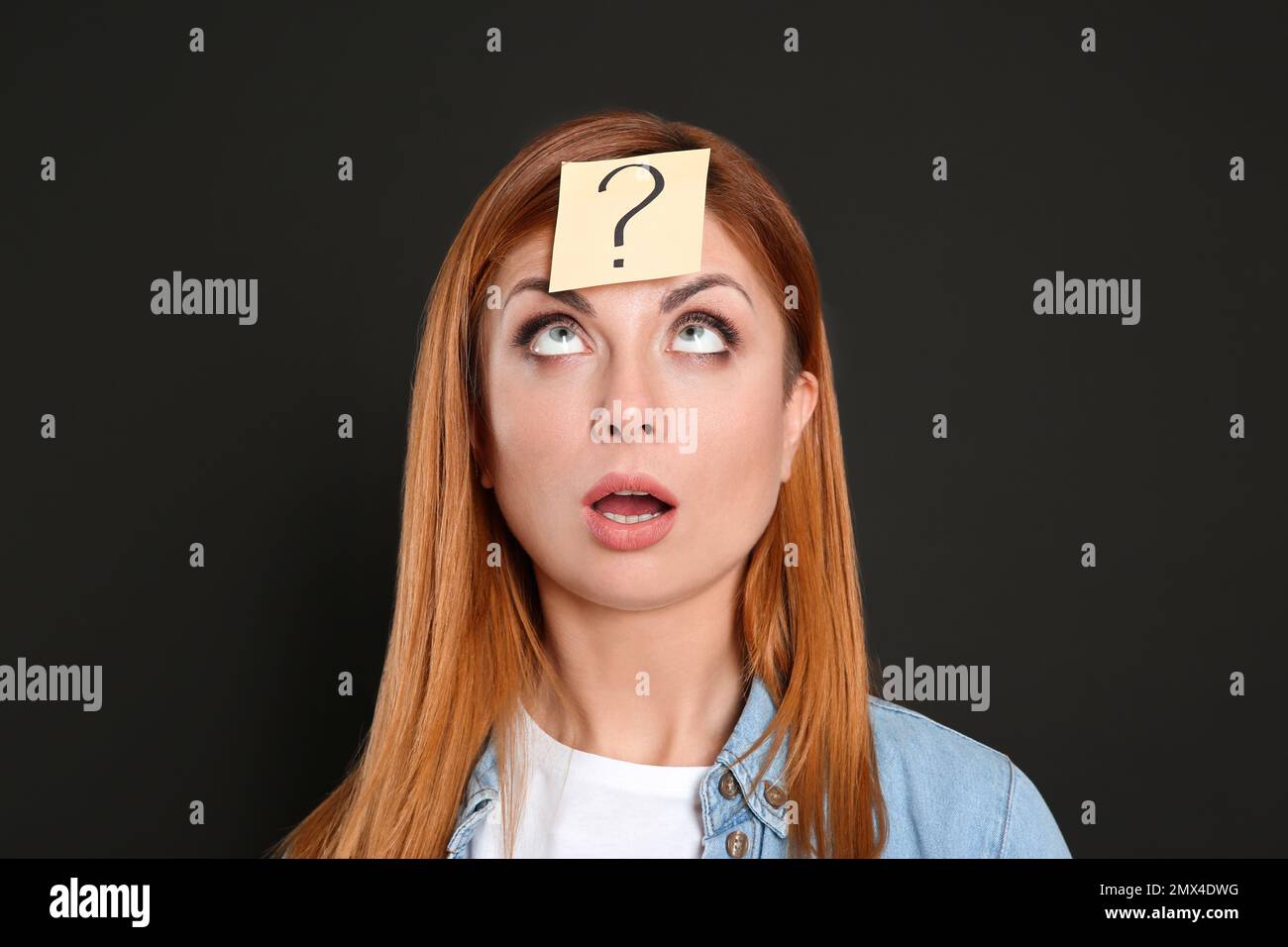 Emotional woman with question mark sticker on forehead against black ...