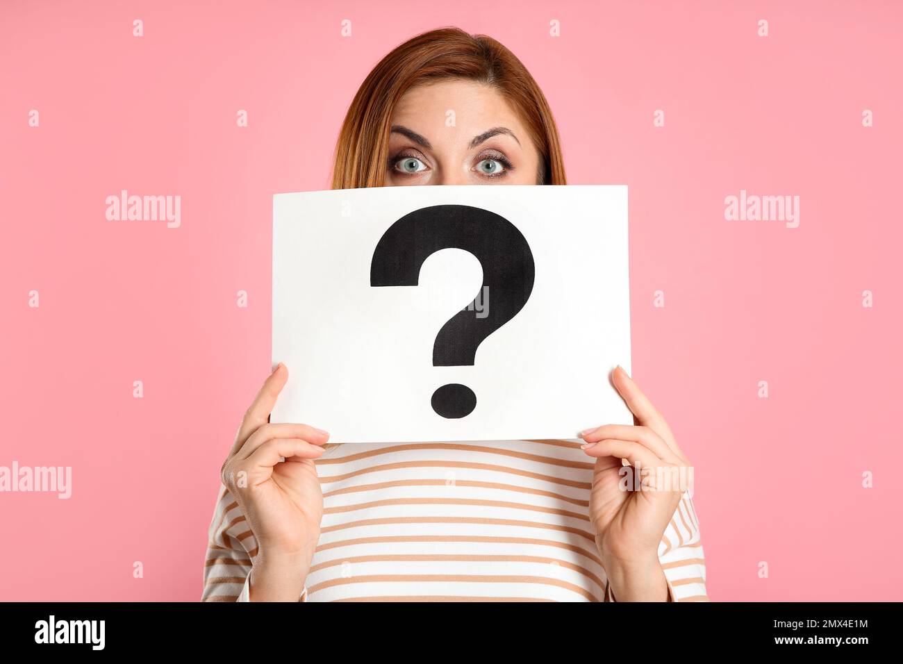 Emotional woman holding question mark sign on pink background Stock ...