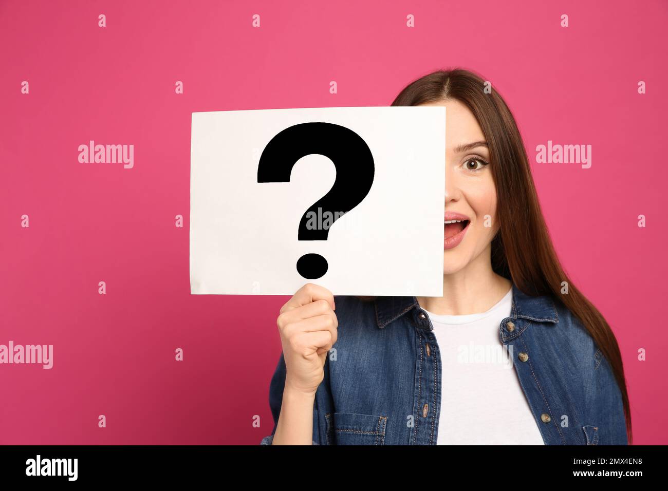 Emotional woman holding question mark sign on pink background Stock ...
