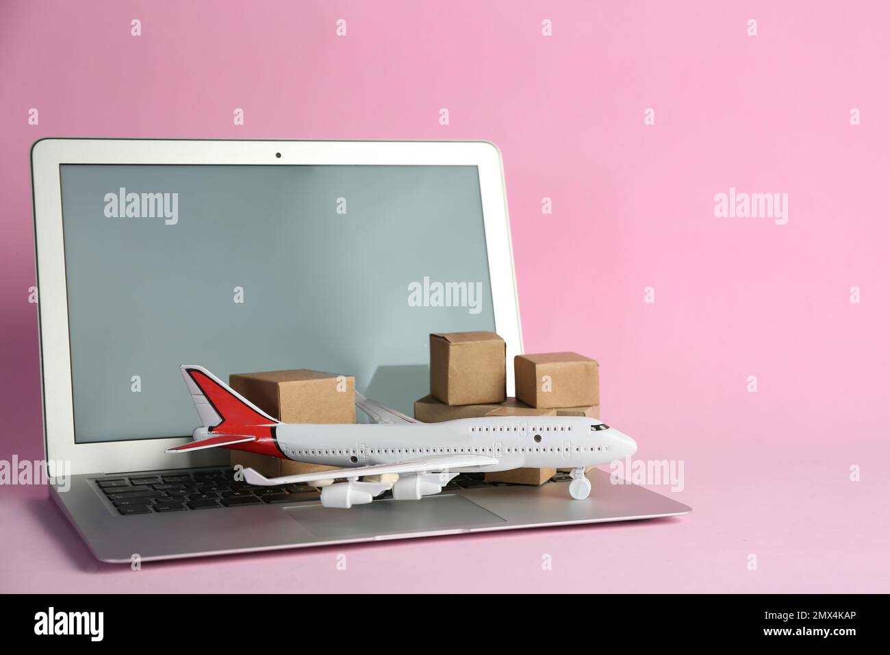 Laptop, airplane model and carton boxes on pink background. Courier ...