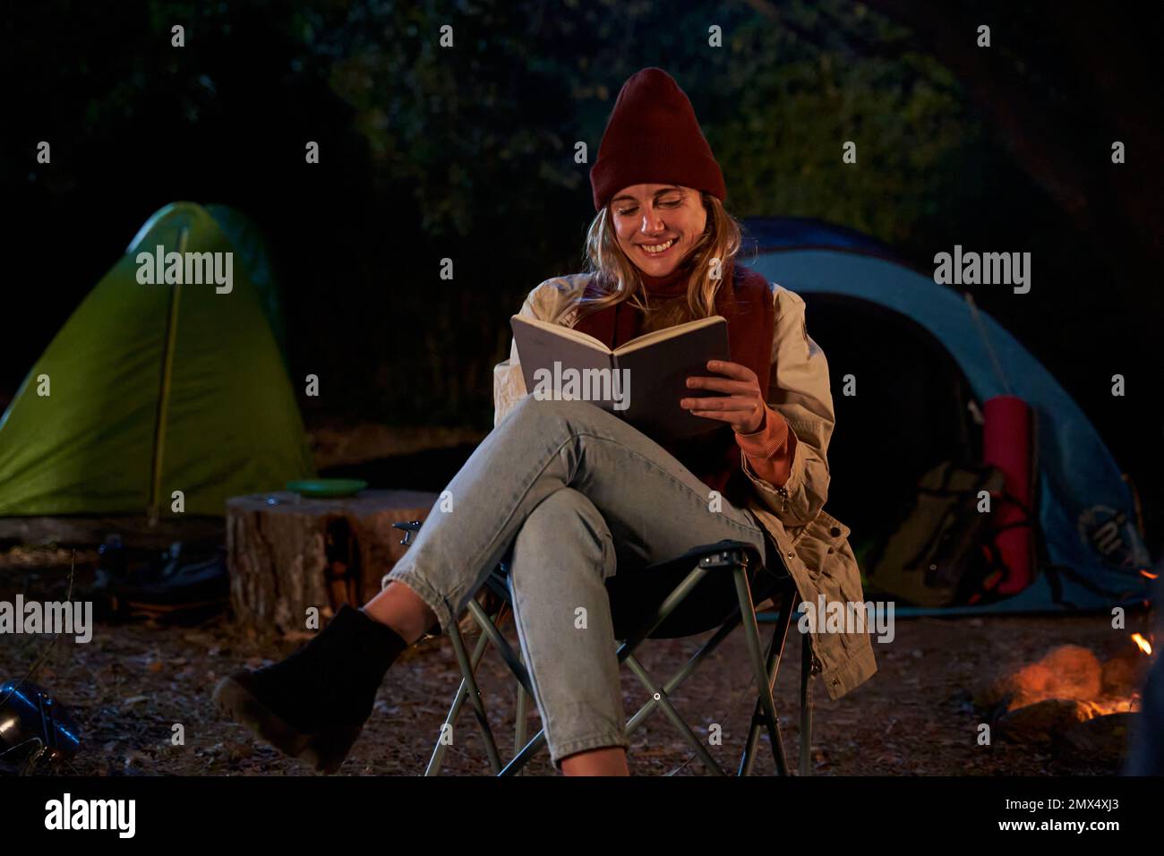 Woman at camping sitting outside at night reading a book, disconnecting ...