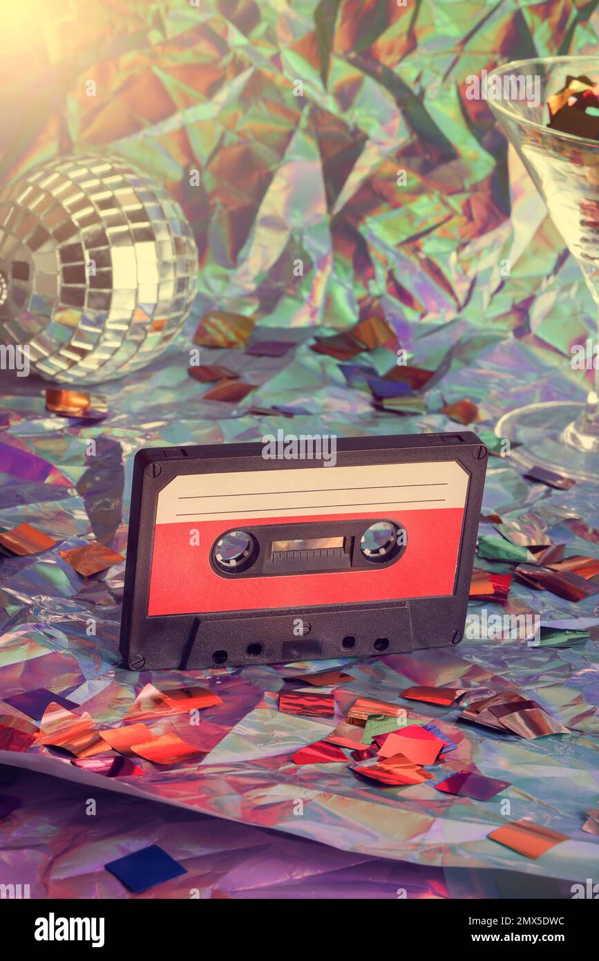 old cassette tape, disco ball and cocktail glass on crumpled neon ...