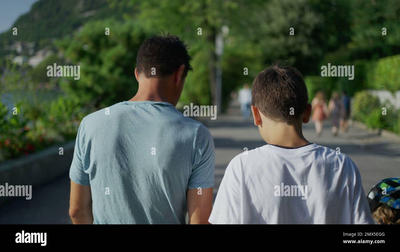 Back of father walking with teen son in beautiful green park. Parent ...