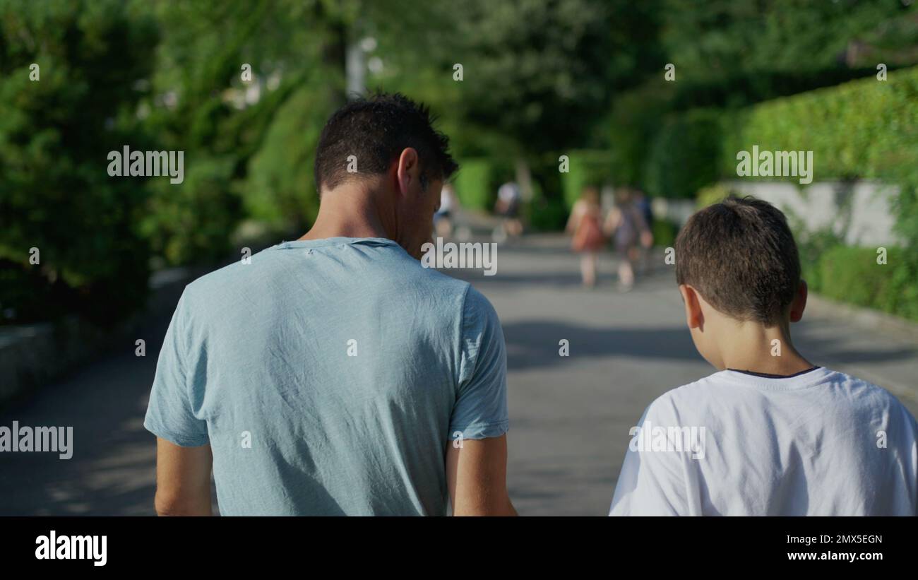 Back of father walking with teen son in beautiful green park. Parent ...