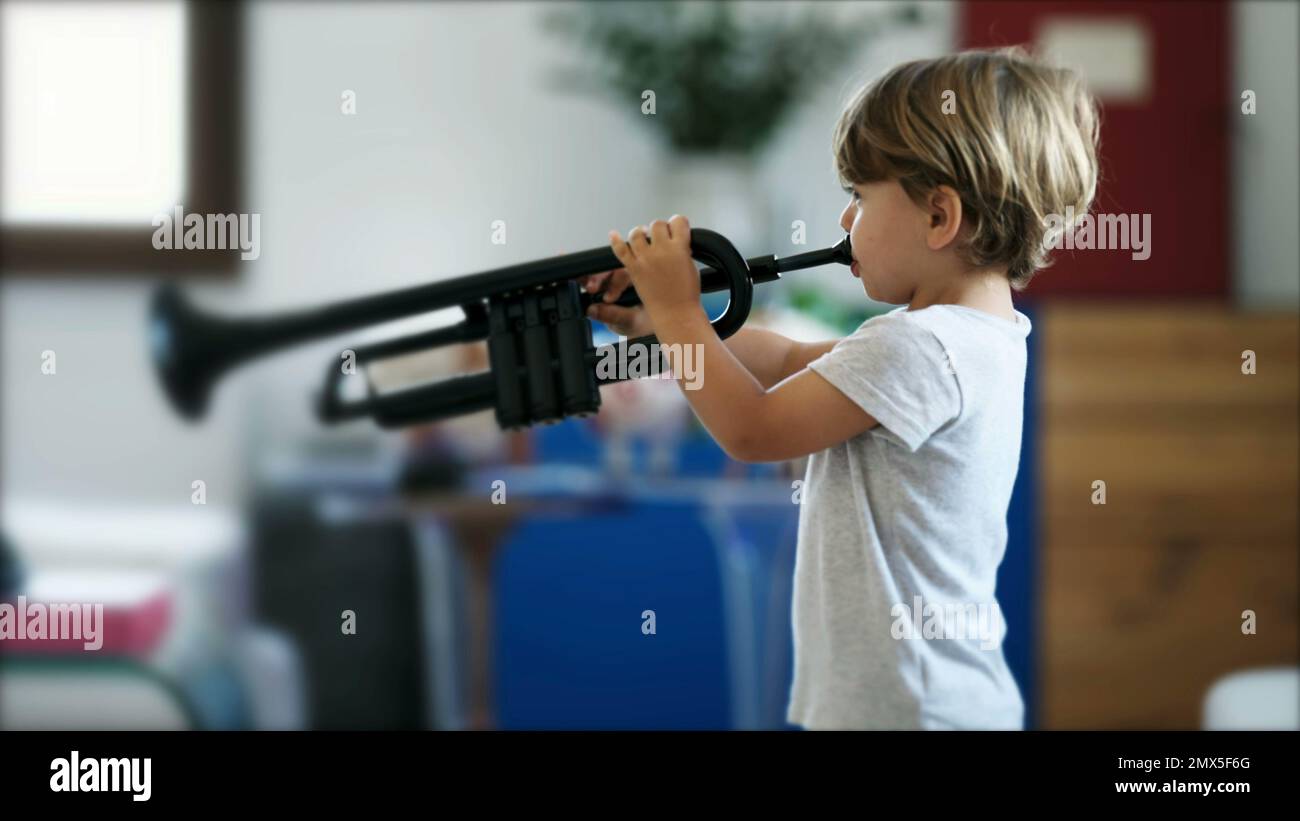 One small boy playing musical instrument. Child plays trumpet indoors ...