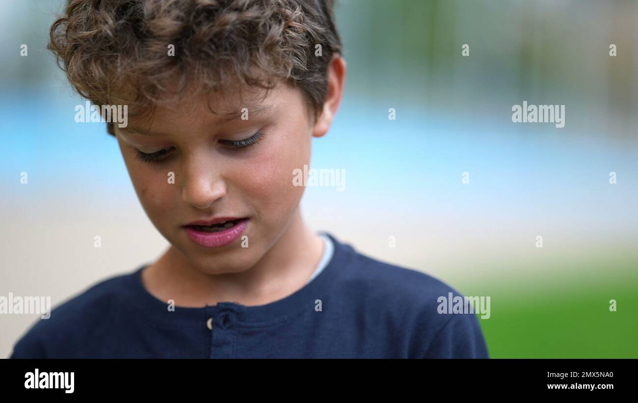 Portrait of a pensive young boy standing outside looking down in ...