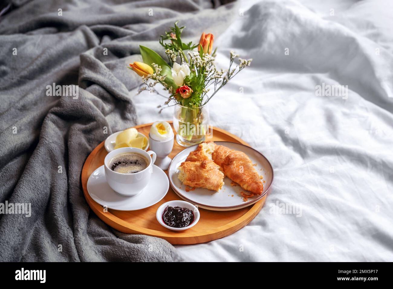 Wooden breakfast tray with croissant, coffee, jam, egg and a fresh ...