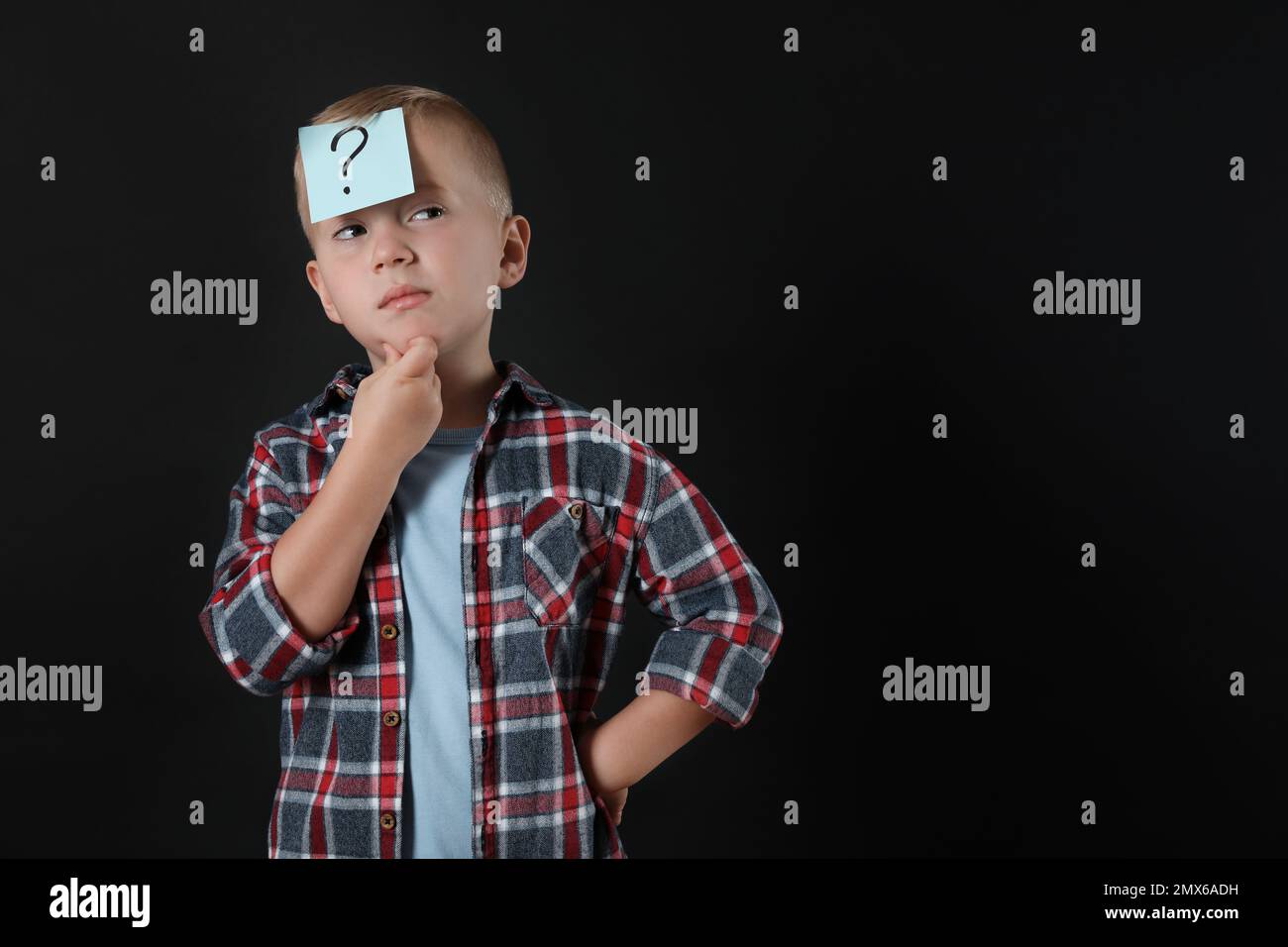 Pensive boy with question mark sticker on forehead against black ...