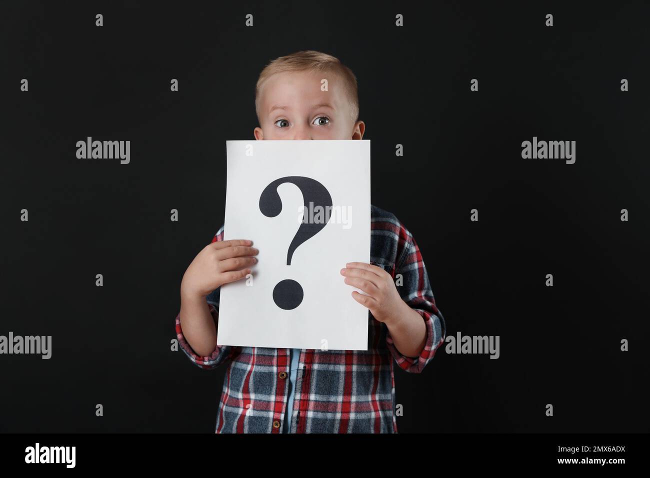 Boy holding sheet of paper with question mark on black background Stock ...
