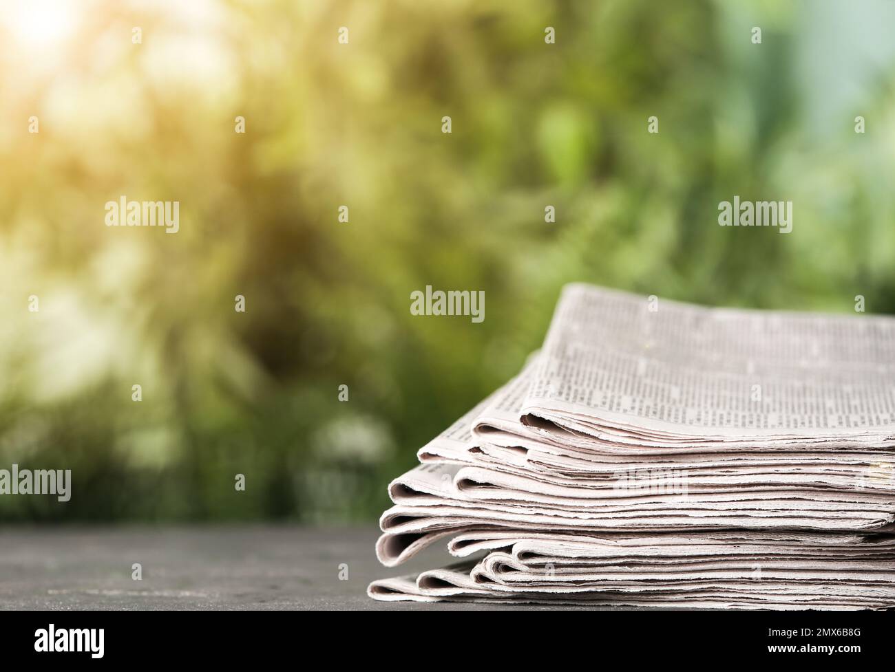 Stack of newspapers on grey table against blurred green background ...