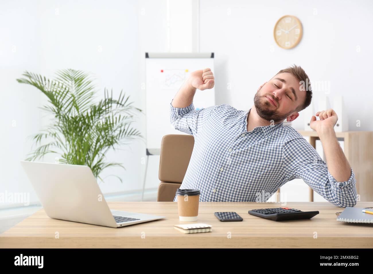 Lazy young office employee stretching at workplace Stock Photo - Alamy