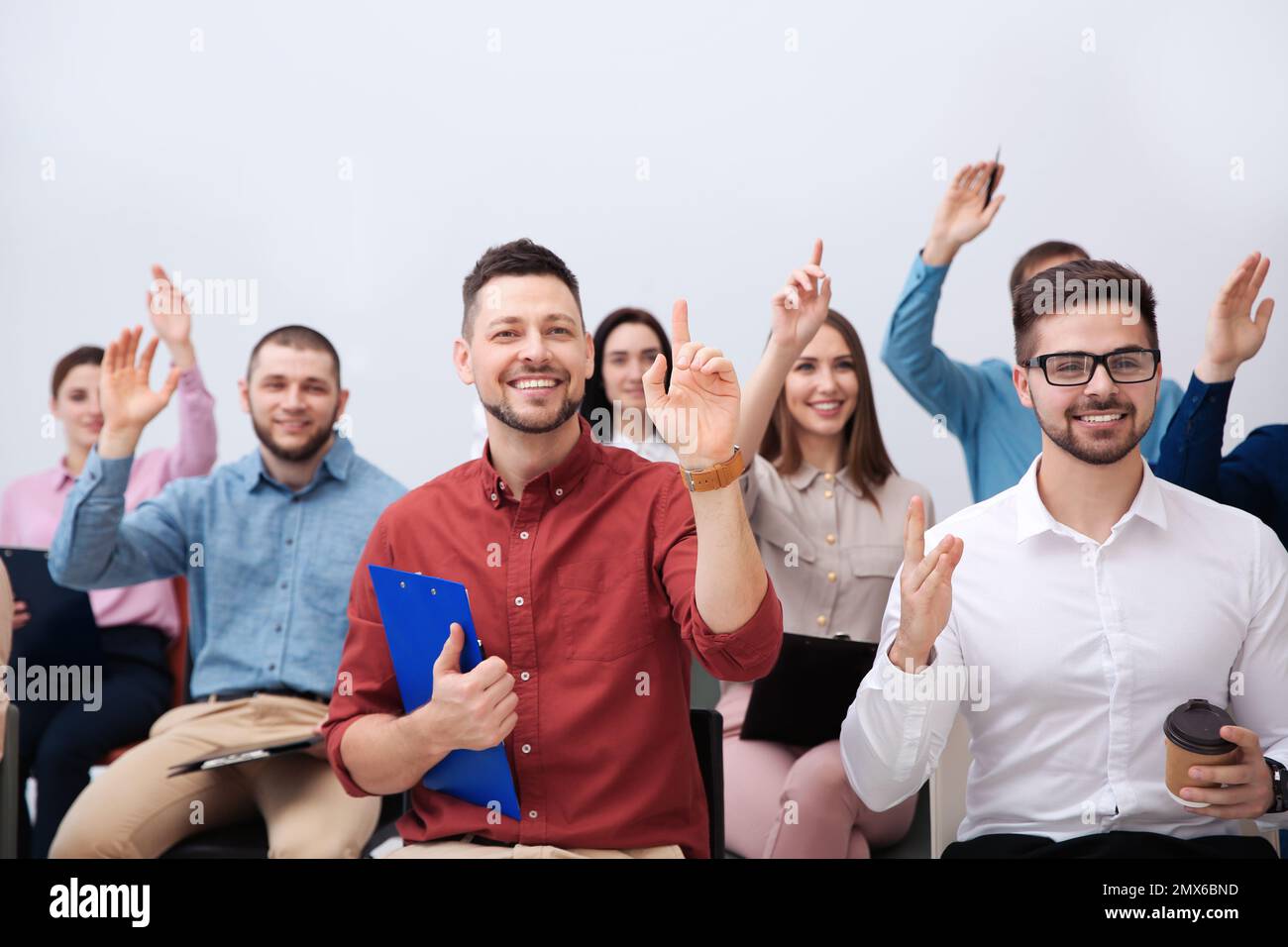 People raising hands to ask questions at business training on white ...