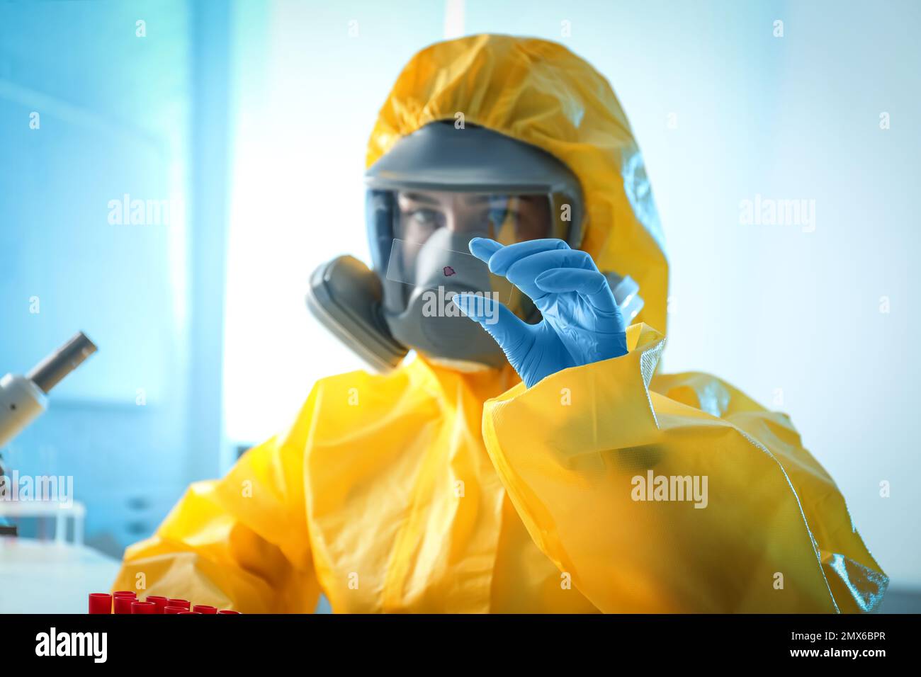 Scientist in chemical protective suit with microscope slide at ...