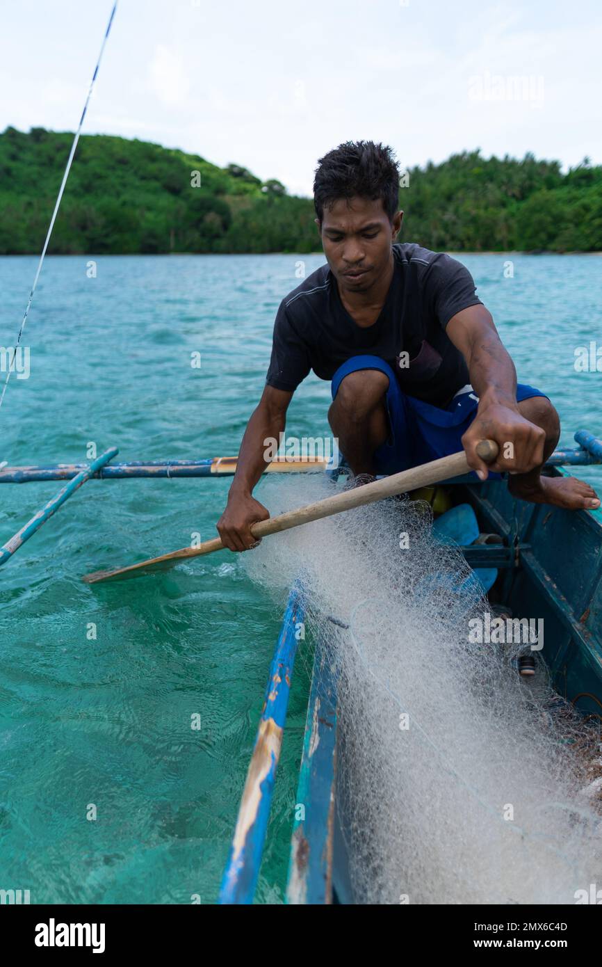 young Filipino fisherman rowing while leaving his fishing net at sea ...