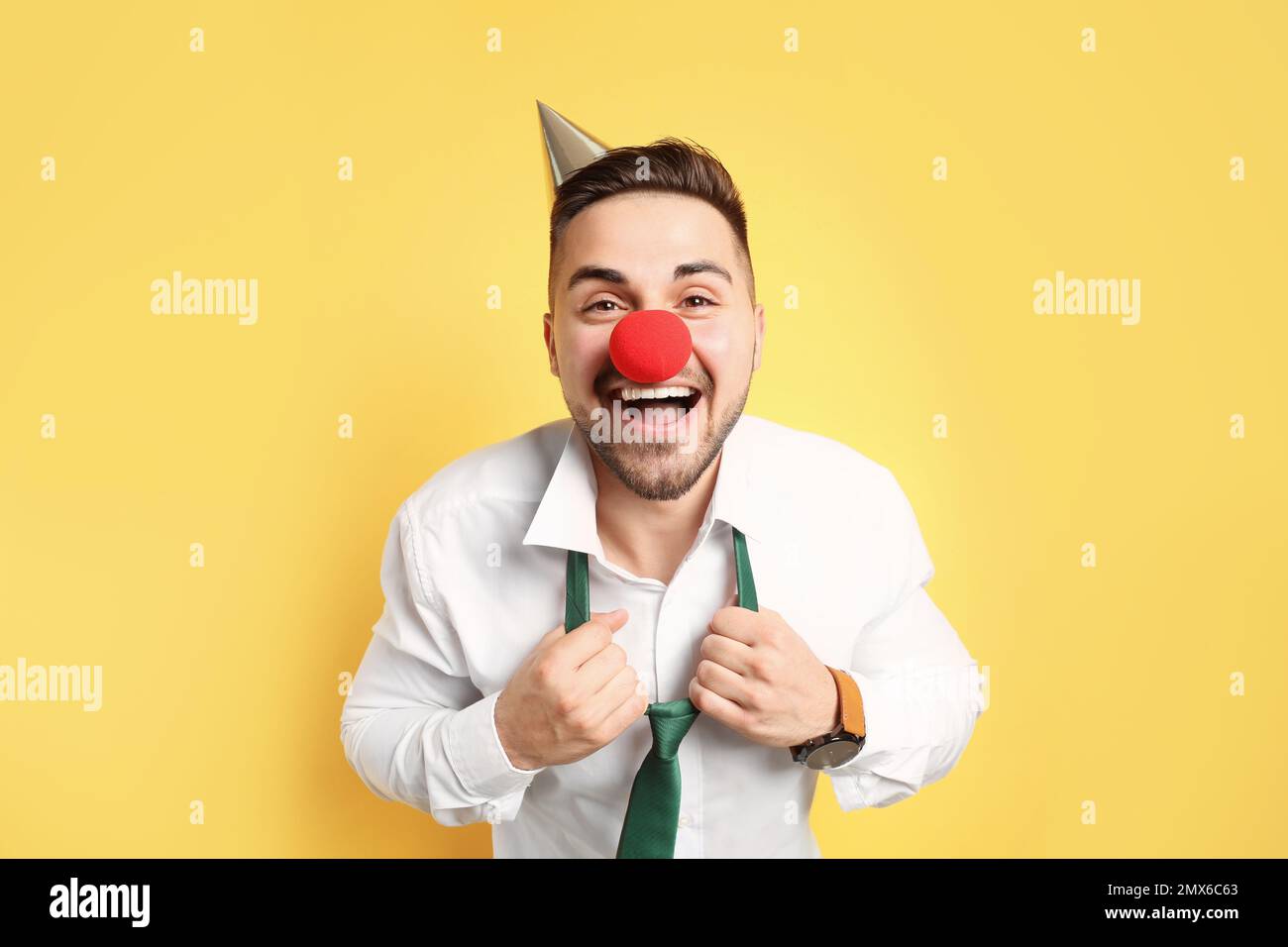 Emotional young man with party cap and clown nose on yellow background ...