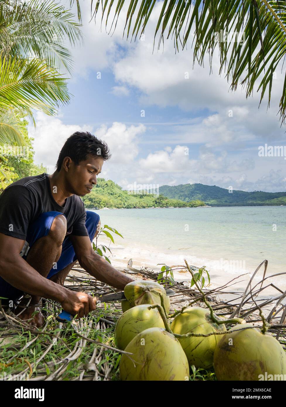 vertical photo of young asian fisherman opening a coconut on a tropical ...