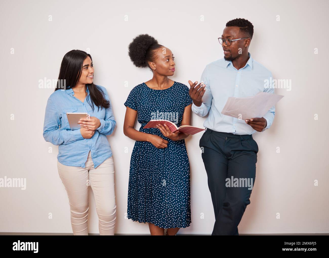 Three coworkers stand and discuss workplace issues with paper, tablet ...
