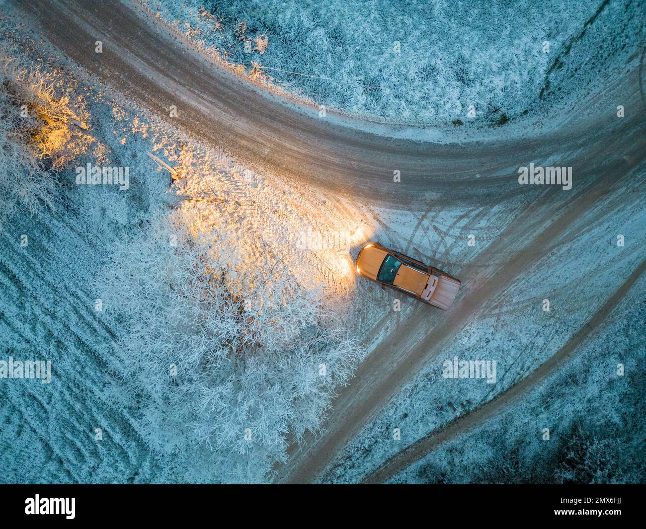 Aerial view of a car driving through a forest at dusk in winter time ...